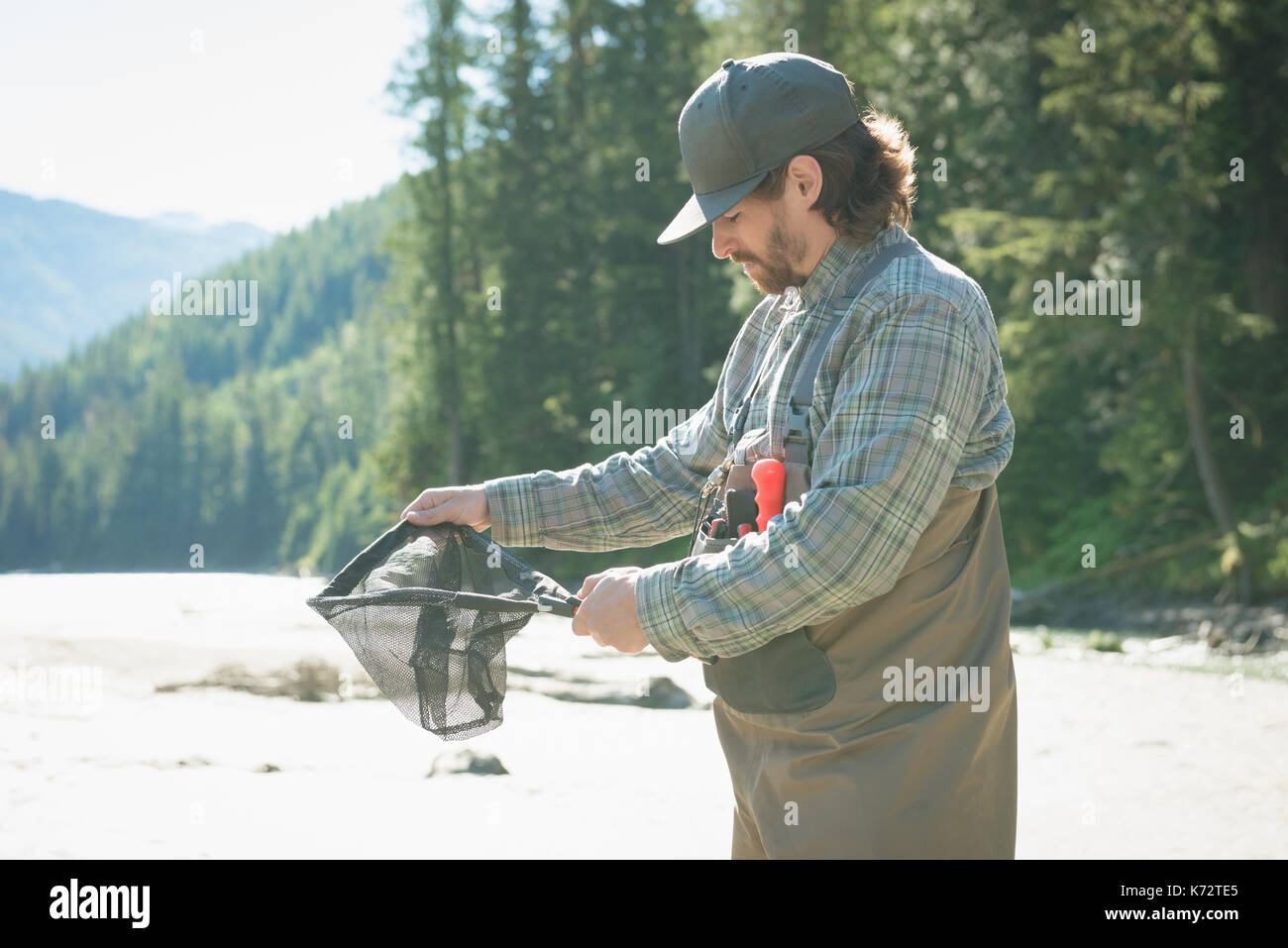Side view of man holding fishing net while standing at riverbank during ...