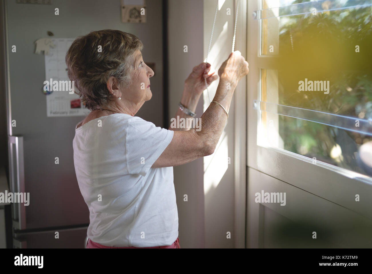 Senior woman opening window shade at home Stock Photo - Alamy