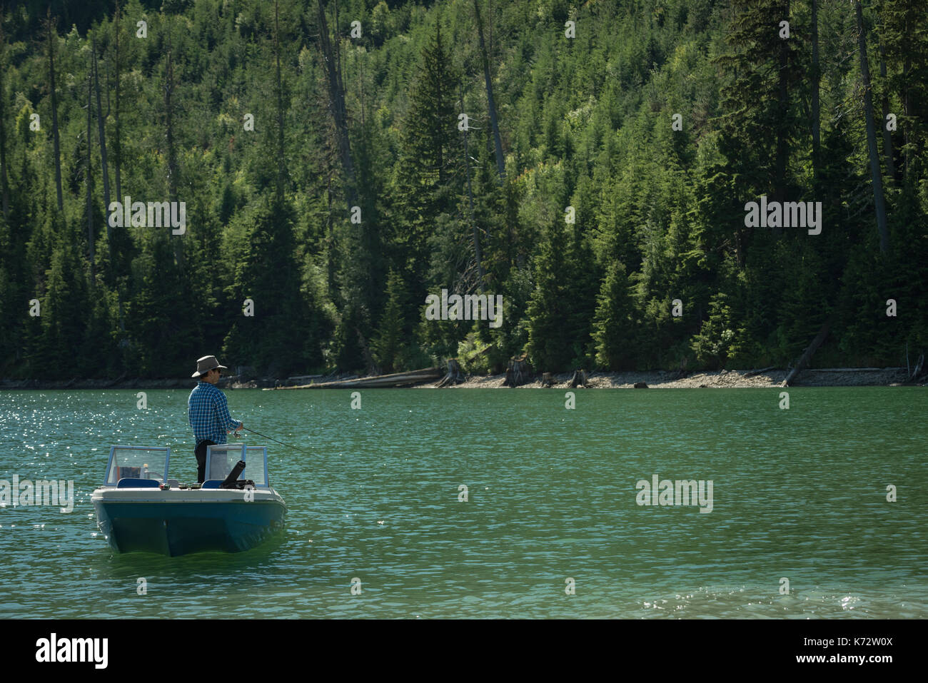 Side view of man fishing while standing on boat in river against tree ...
