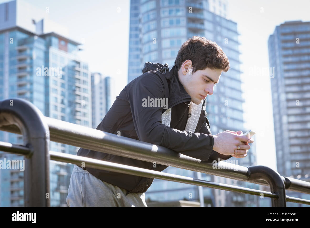 Young man using phone while leaning on railing against buildings during ...