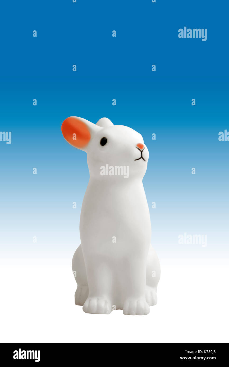 a cute white plastic bunny on a blue gradient background. Minimal color ...