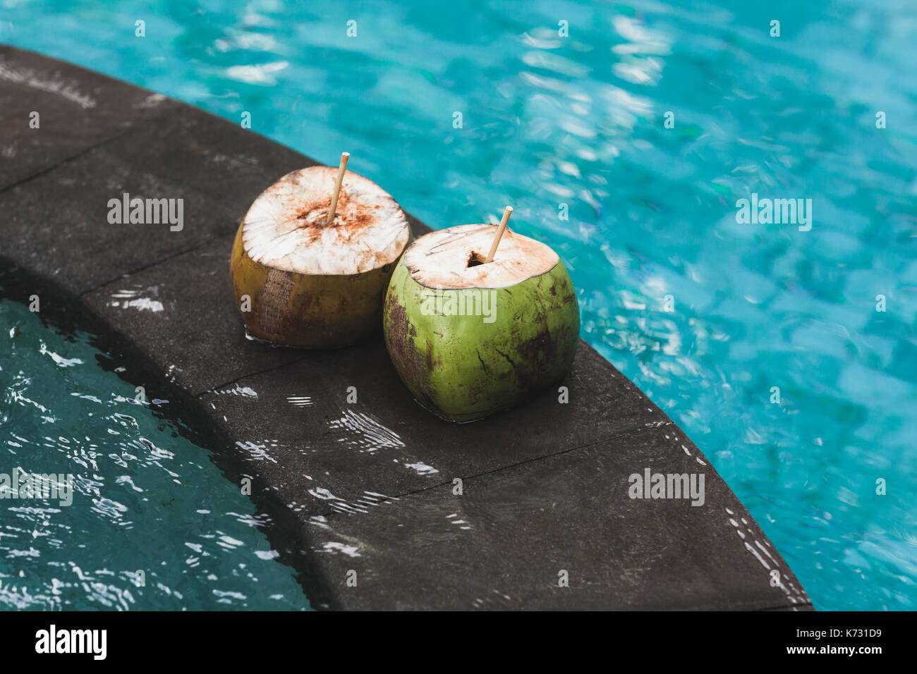 Two young fresh coconuts on edge of swimming pool with crystal clean ...