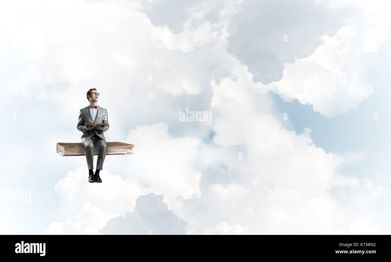 Young businessman or student floating in blue sky and studying the ...