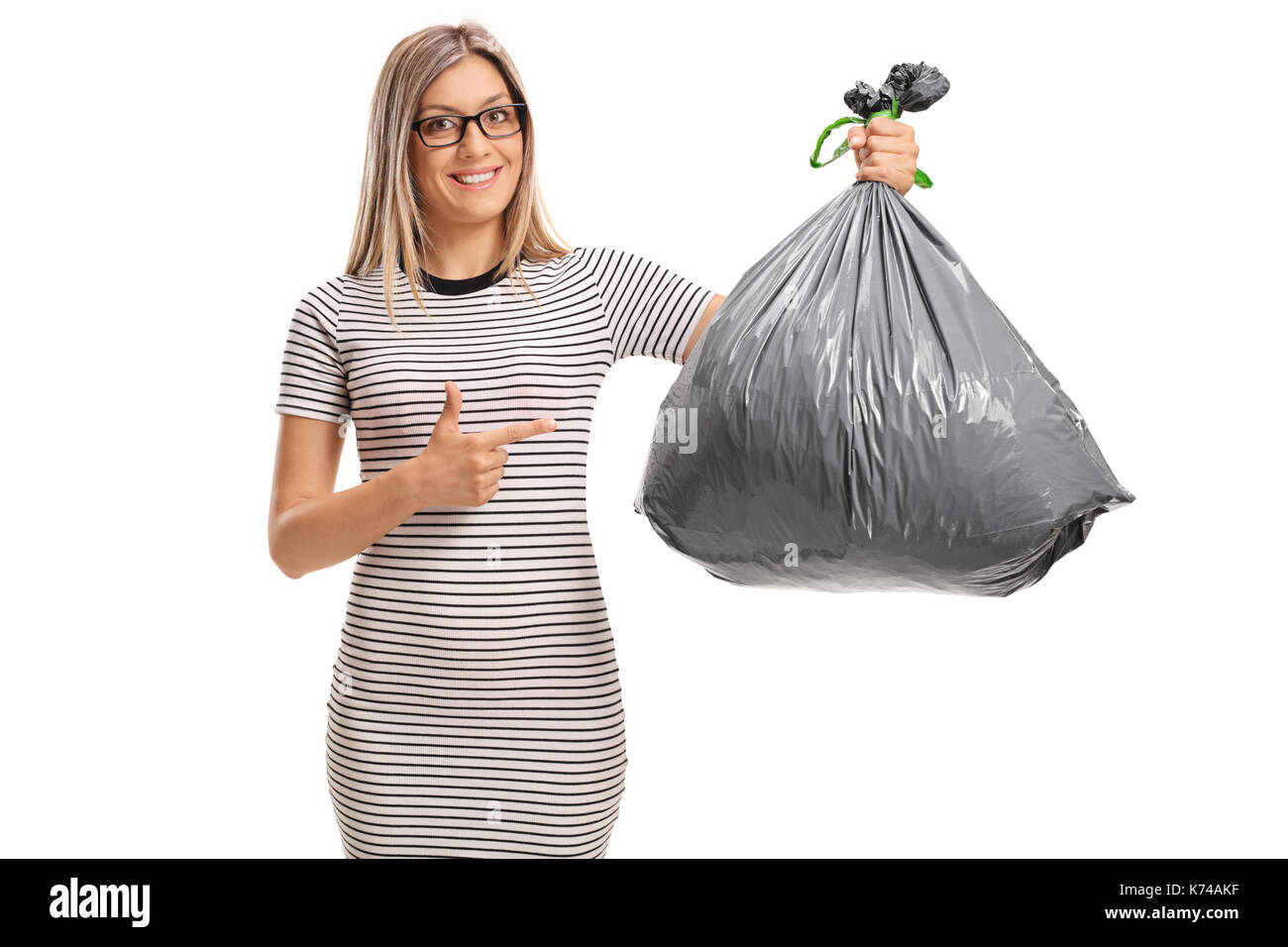 Young woman holding a garbage bag and pointing isolated on white ...