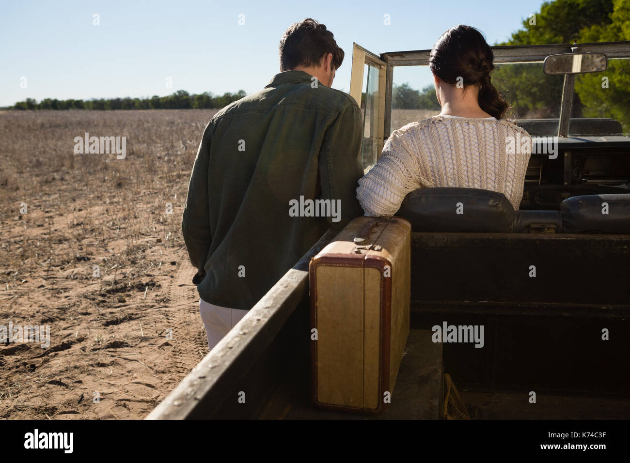 Rear view of man by woman sitting in off road vehicle on landscape ...