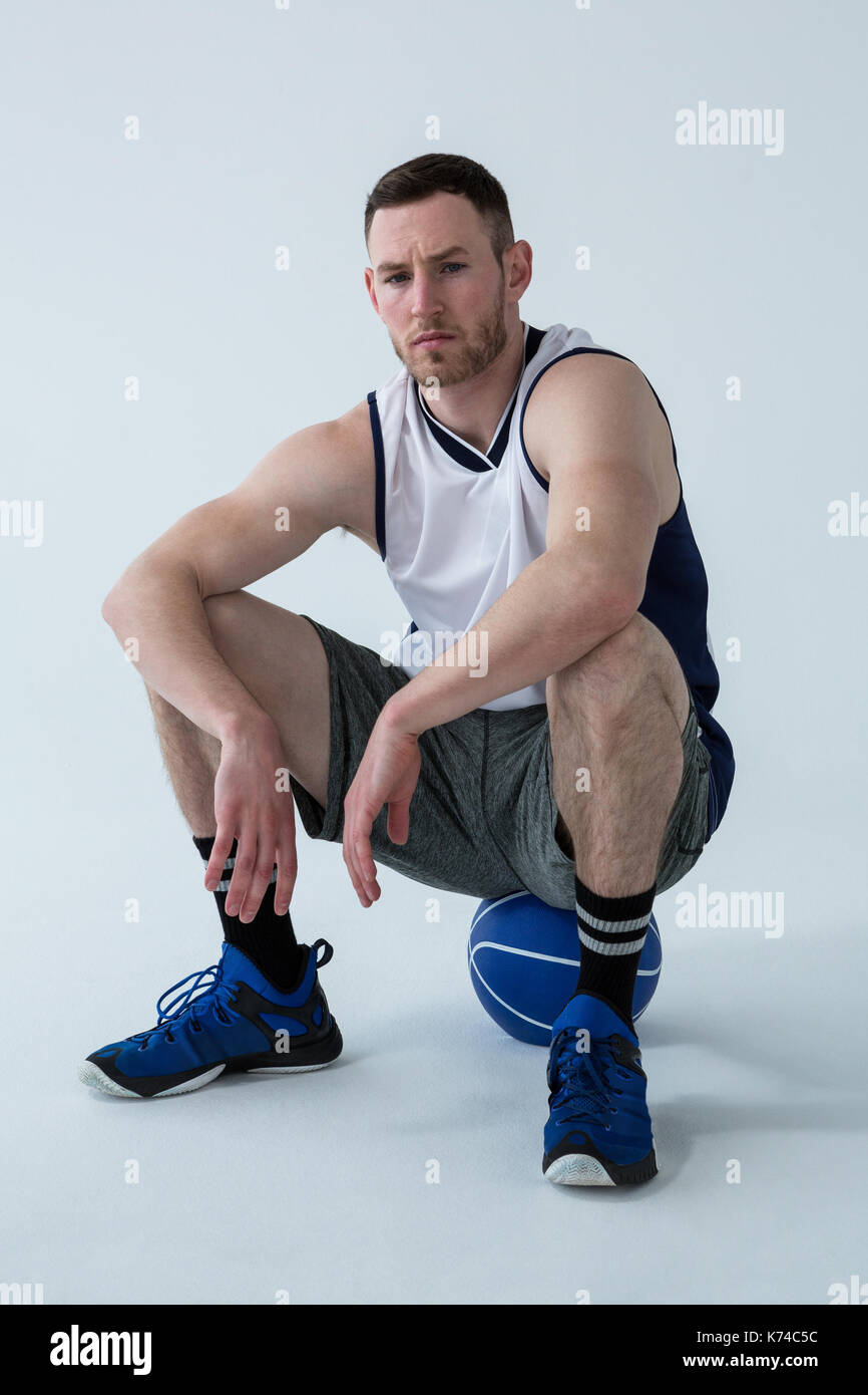 Confident player sitting on basketball against white background Stock ...