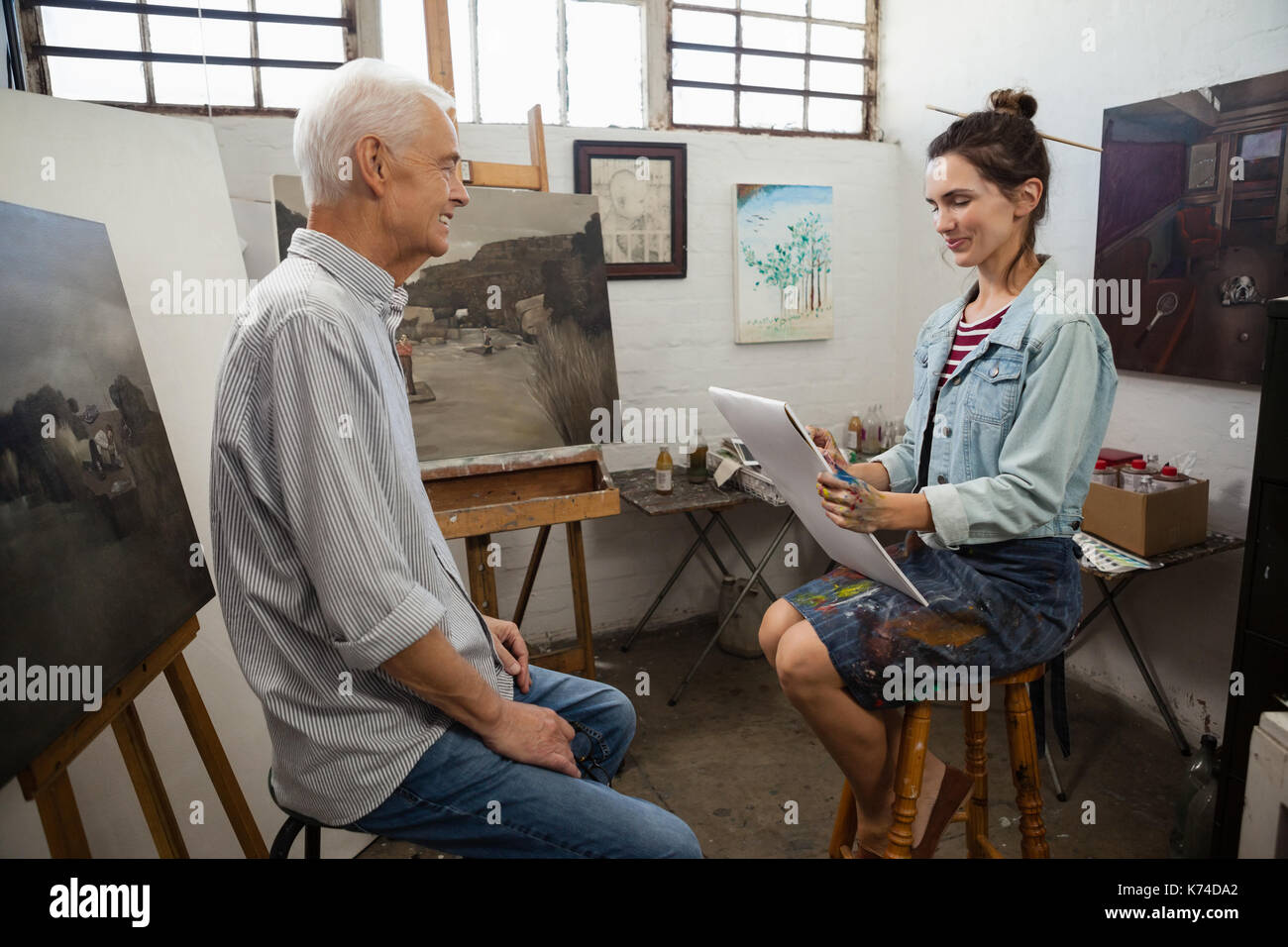 Woman interacting with senior man while sketching on canvas in drawing ...
