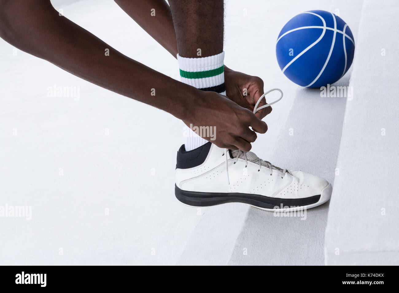 Low section of basketball player tying shoelace on white background ...