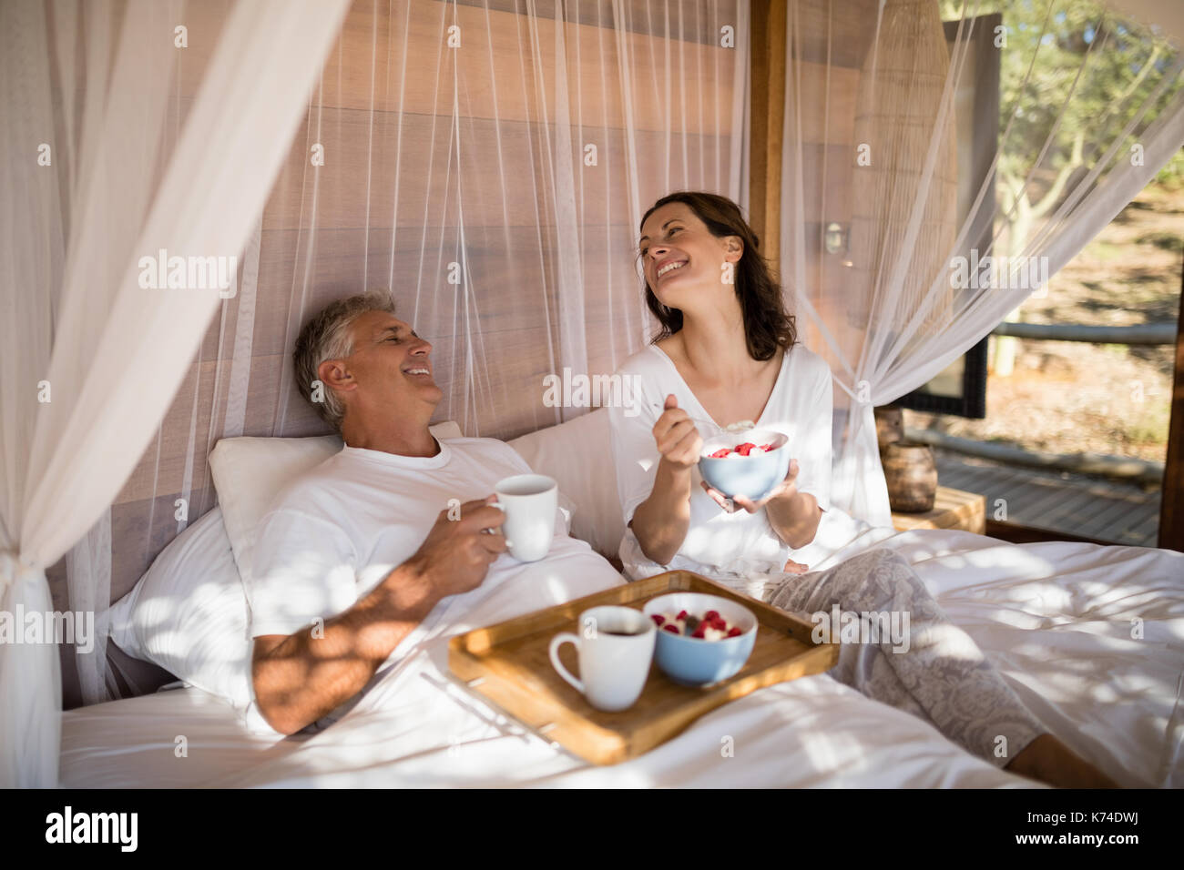 Happy couple having breakfast in canopy bed during morning Stock Photo ...
