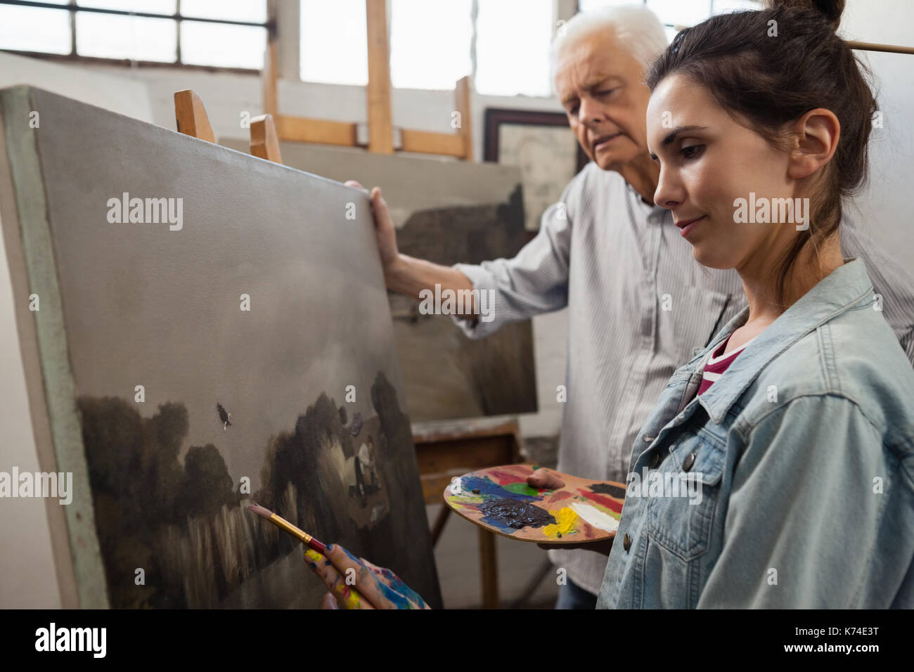 Senior man watching while artist painting on canvas in drawing class ...