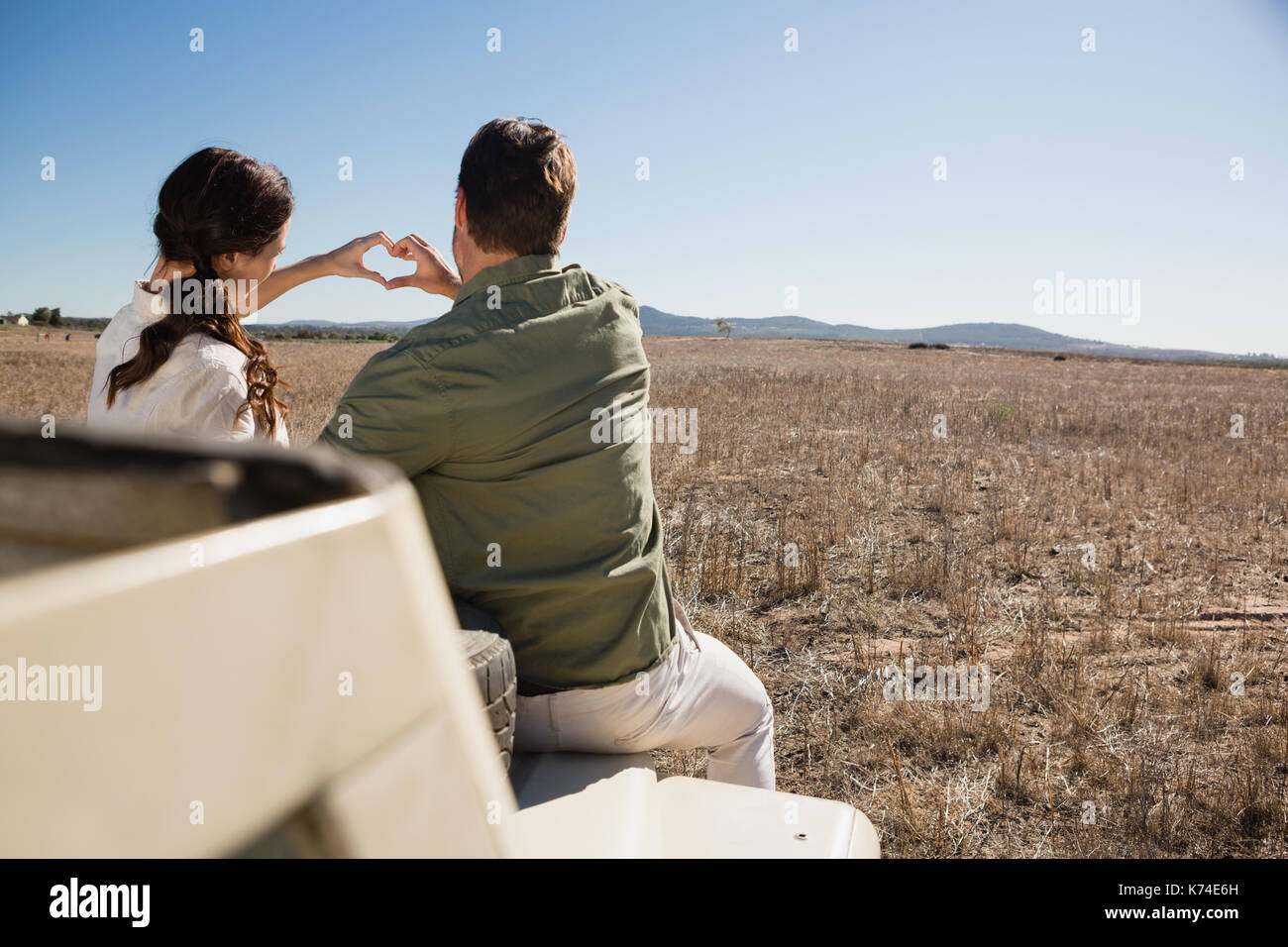 Rear view of young couple making heart shape with hands on off road ...