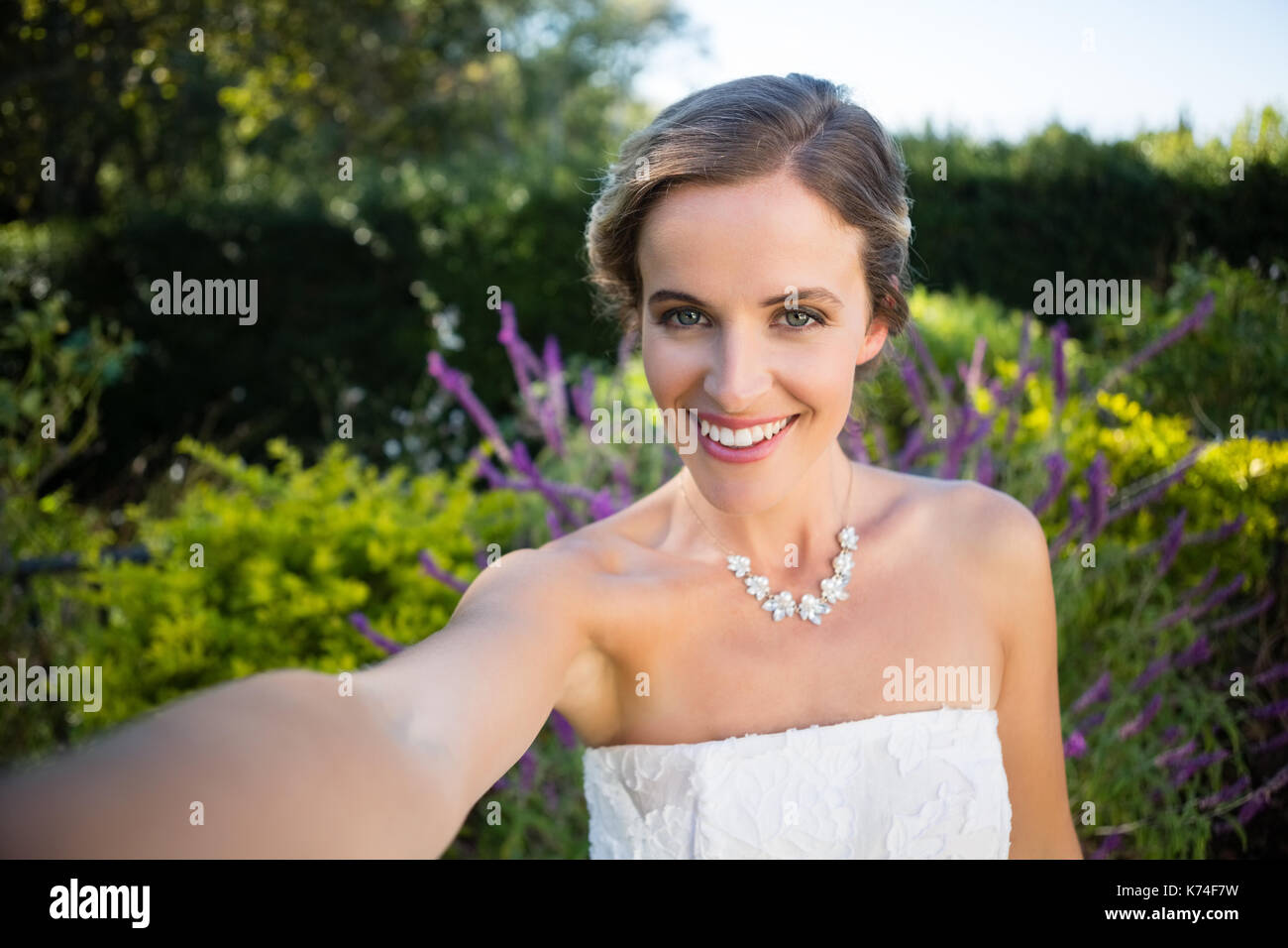 Portrait of smiling beautiful bride standing against plants in yard ...