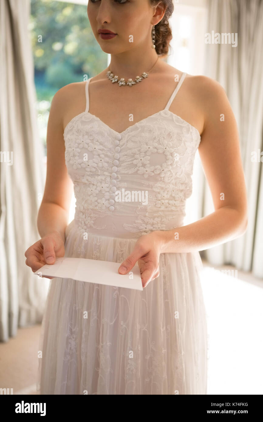 Beautiful bride holding wedding card while standing at home Stock Photo ...