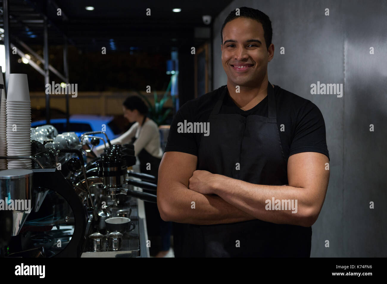 Portrait of waiter standing with arms crossed at counter in restaurant ...
