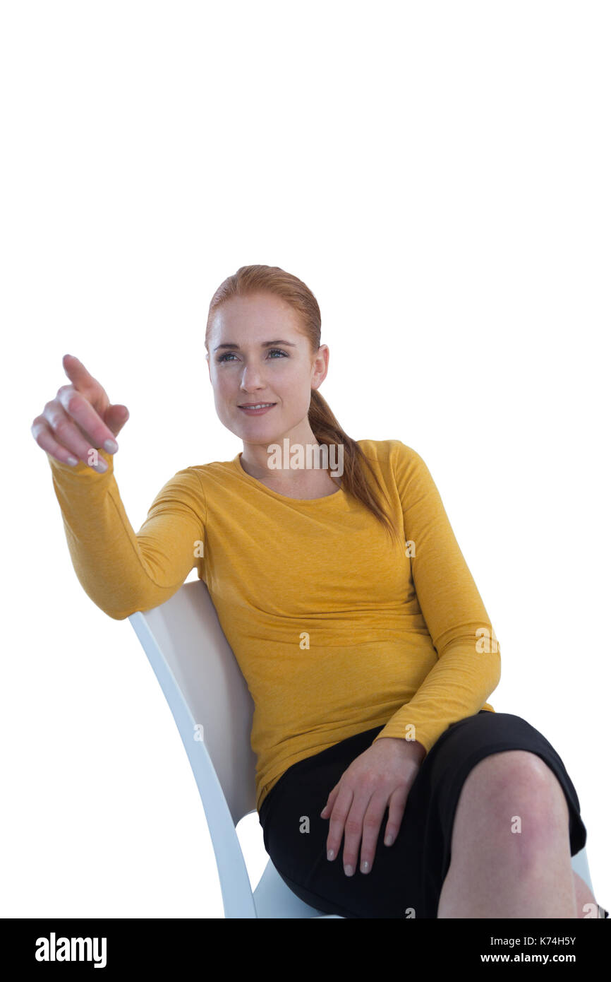 Confident businesswoman pointing while sitting on chair against white ...
