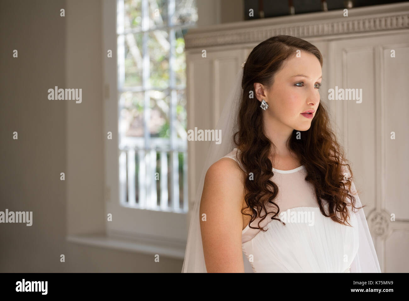 Thoughtful bride wearing wedding dress looking away while standing at ...