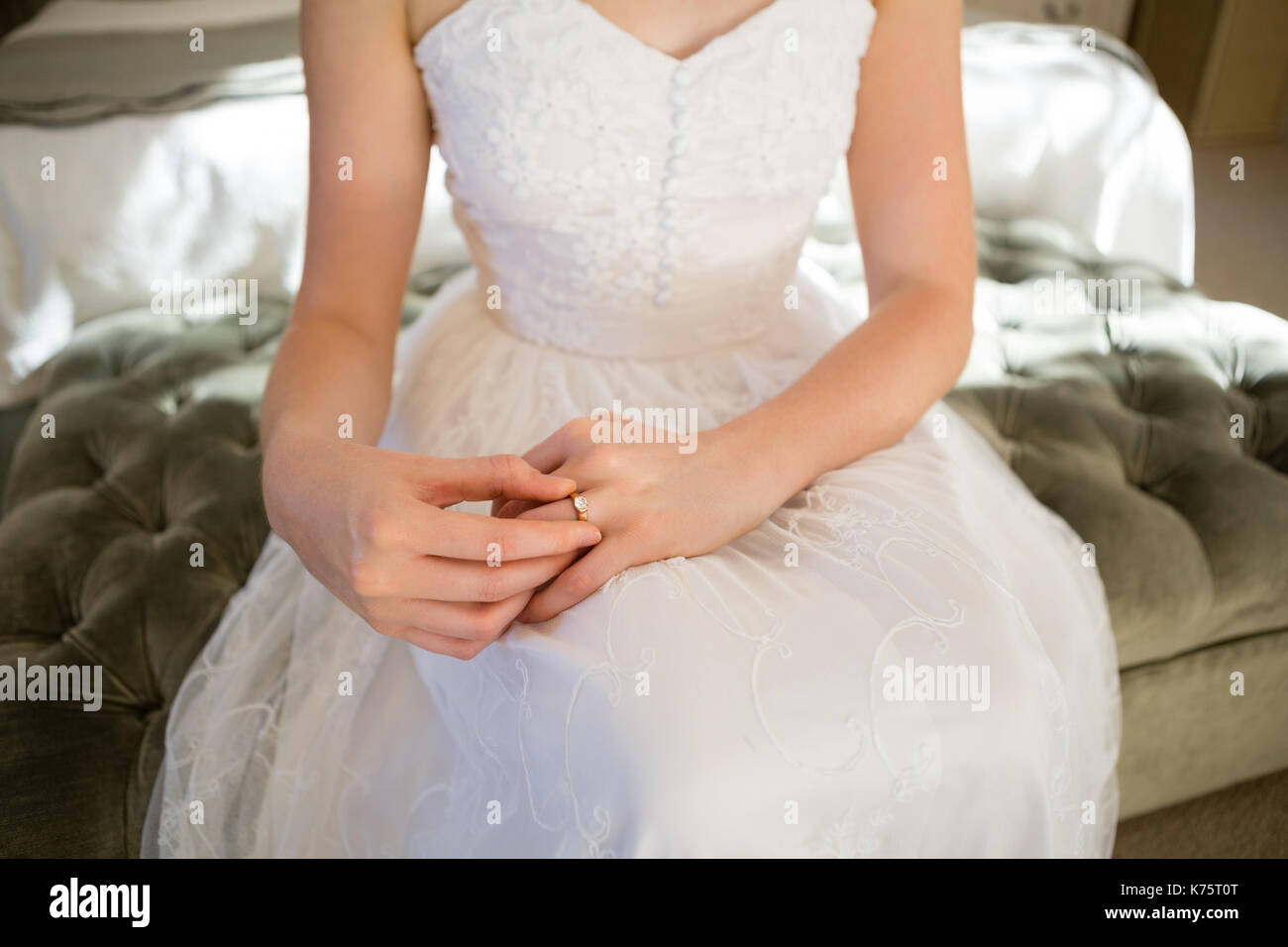 Midsection of bride trying wedding ring while sitting on bed at home ...
