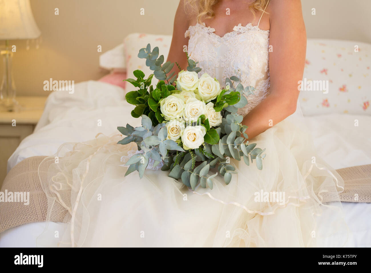 Midsection of bride in wedding dress holding bouquet while sitting on ...