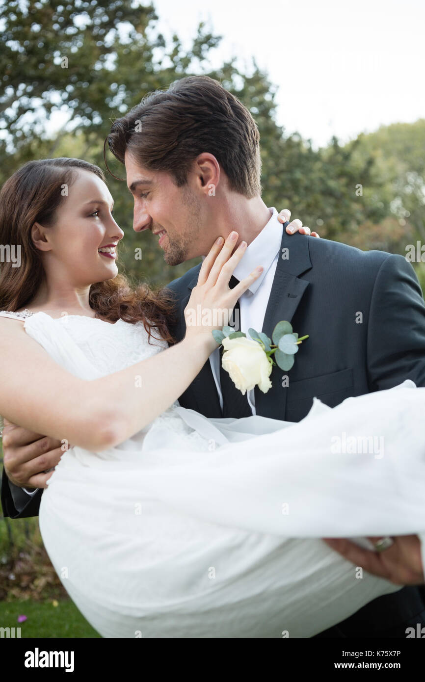 Romantic bridegroom carrying bride while standing in park Stock Photo ...