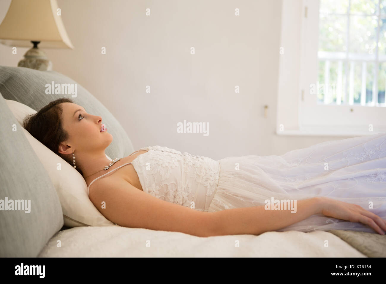 Thoughtful bride looking up while relaxing on bed at home Stock Photo ...
