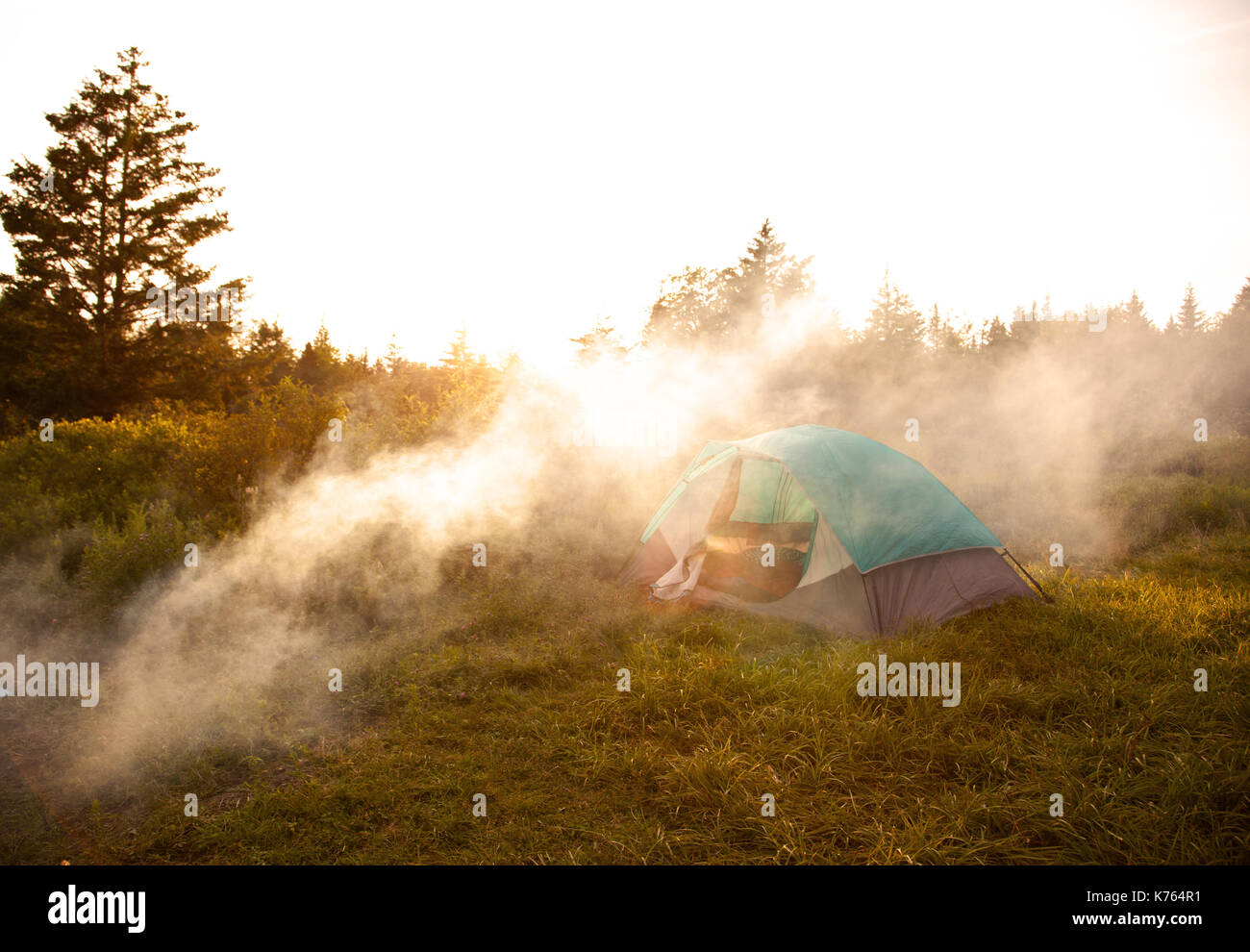 a campfire rolls smoke and haze over a green tent in a field on a ...