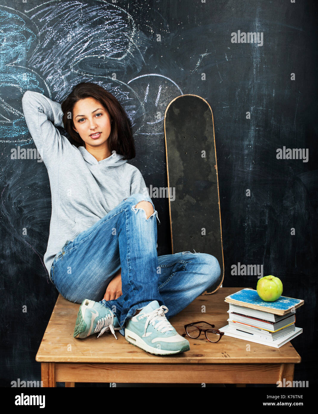 young cute teenage girl in classroom at blackboard seating on table ...