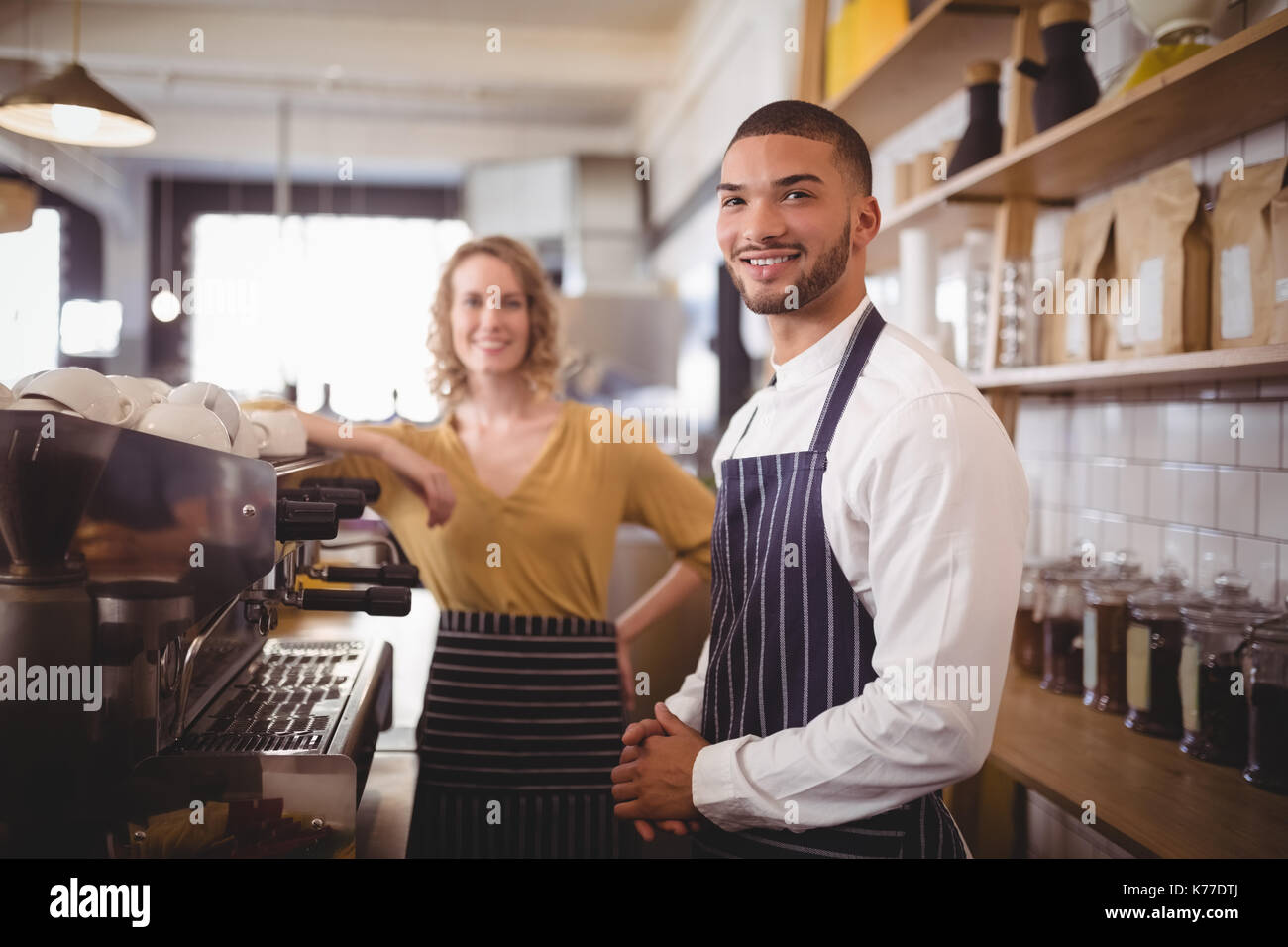 Portrait of smiling young waiter and waitress standing by espresso ...