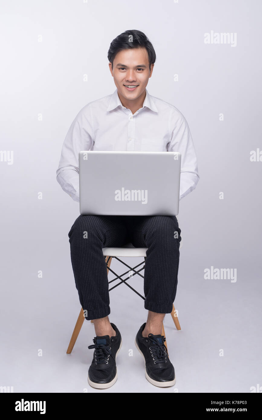 Smart casual asian man seated on chair, using laptop in studio ...