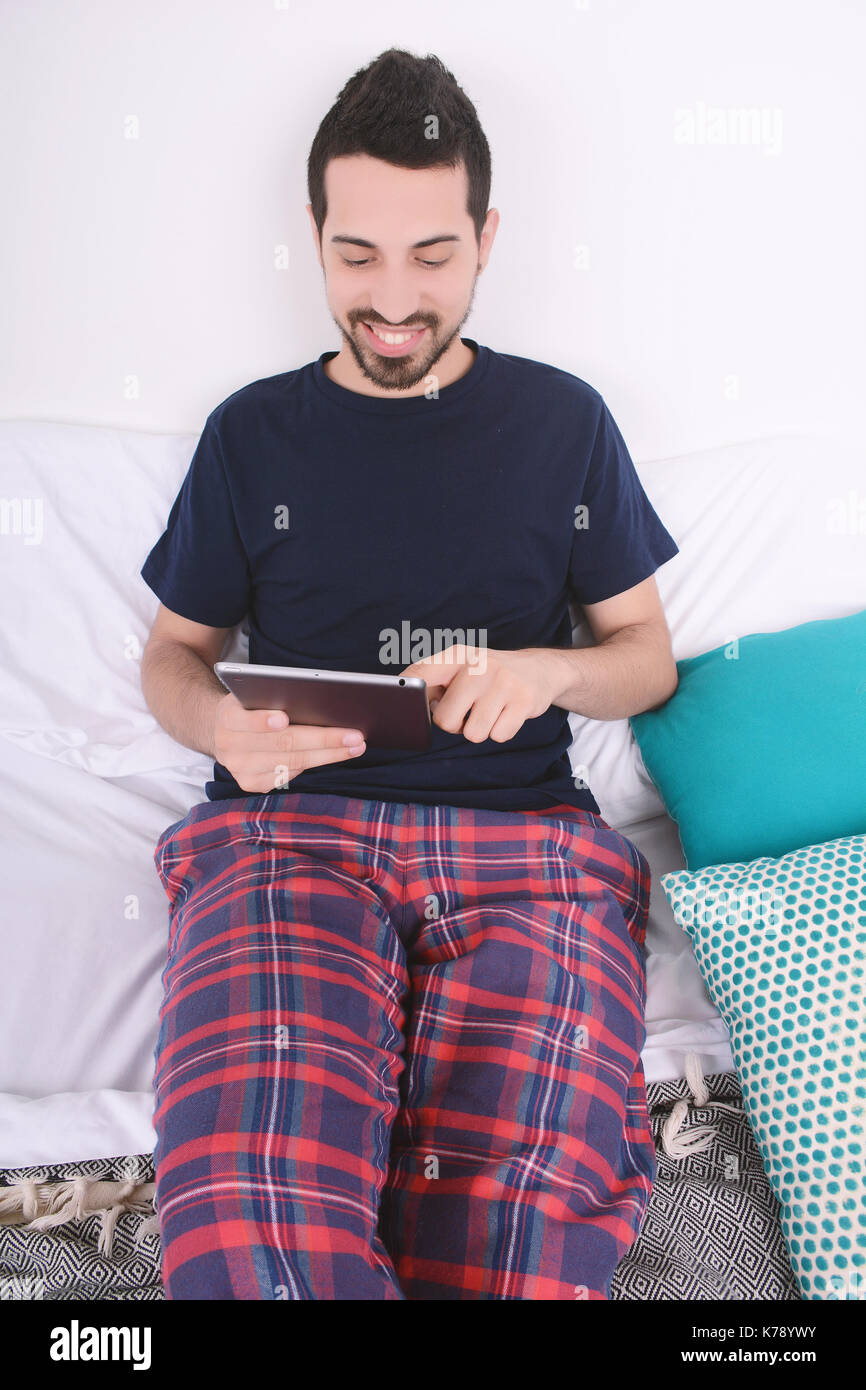 Attractive young man using digital tablet and relaxed on bed. Indoors ...