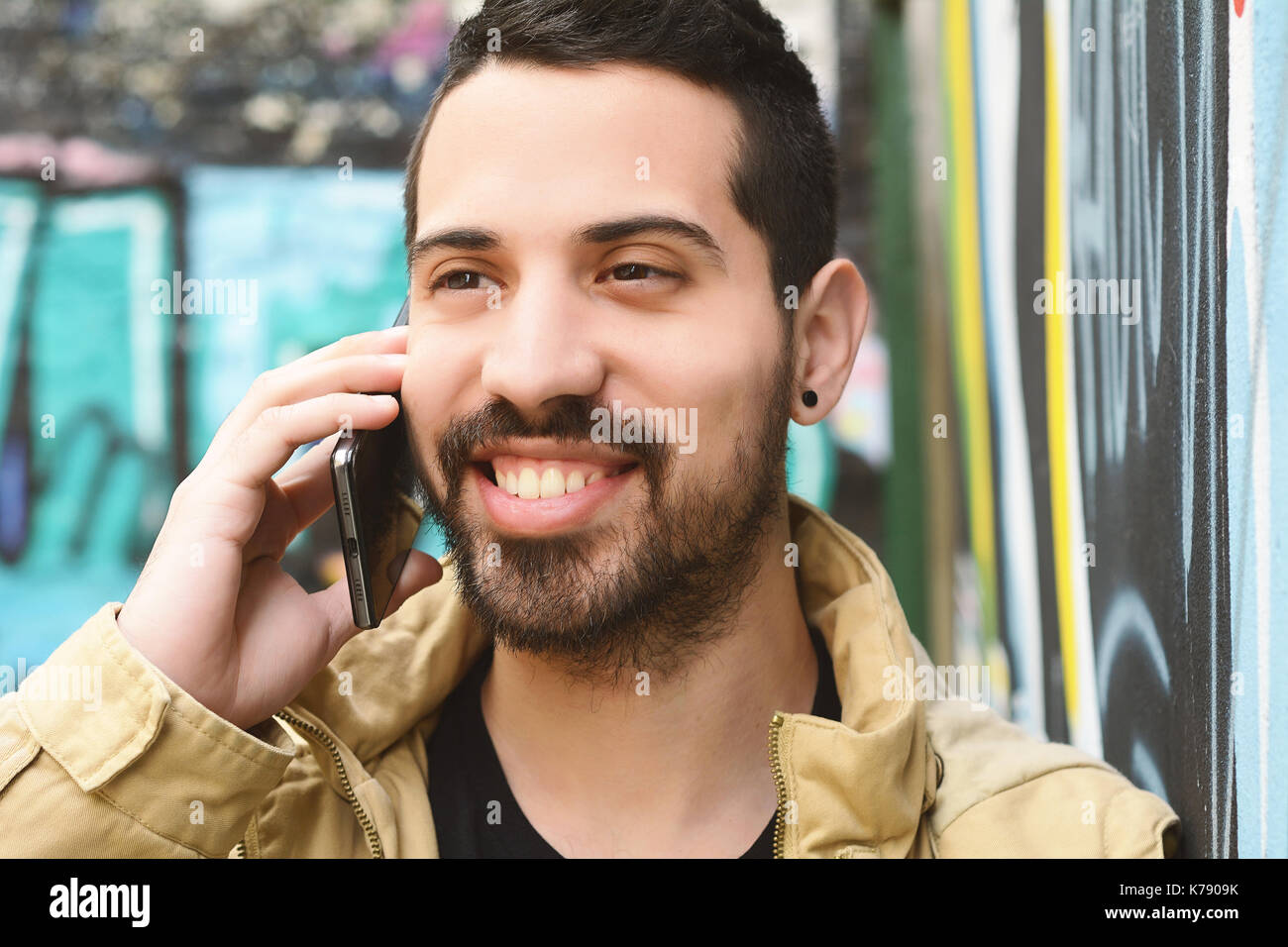 Portrait of young latin man talking on the phone against brick wall ...