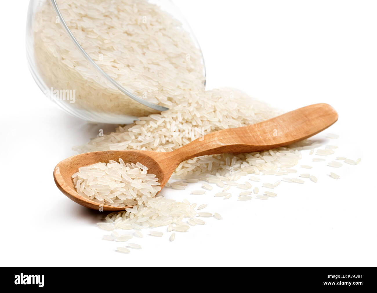 Wooden spoon and glass bowl with scattered rice on white background ...