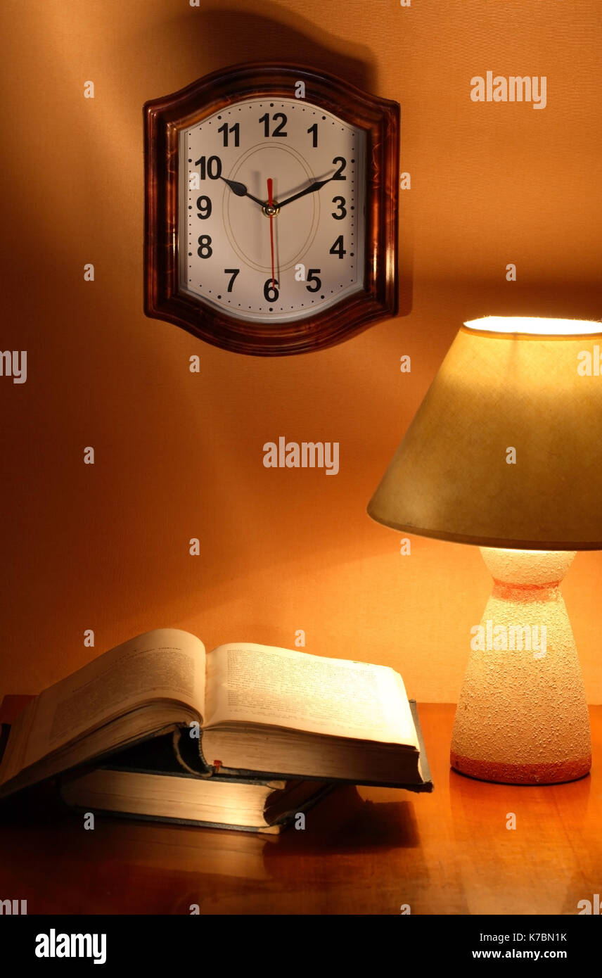 Still life with luminous desk lamp near old books and clock Stock Photo ...