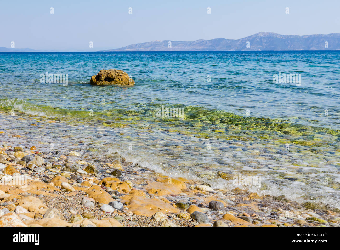Rocky shore with boulder sticking out of shallow water surface with ...