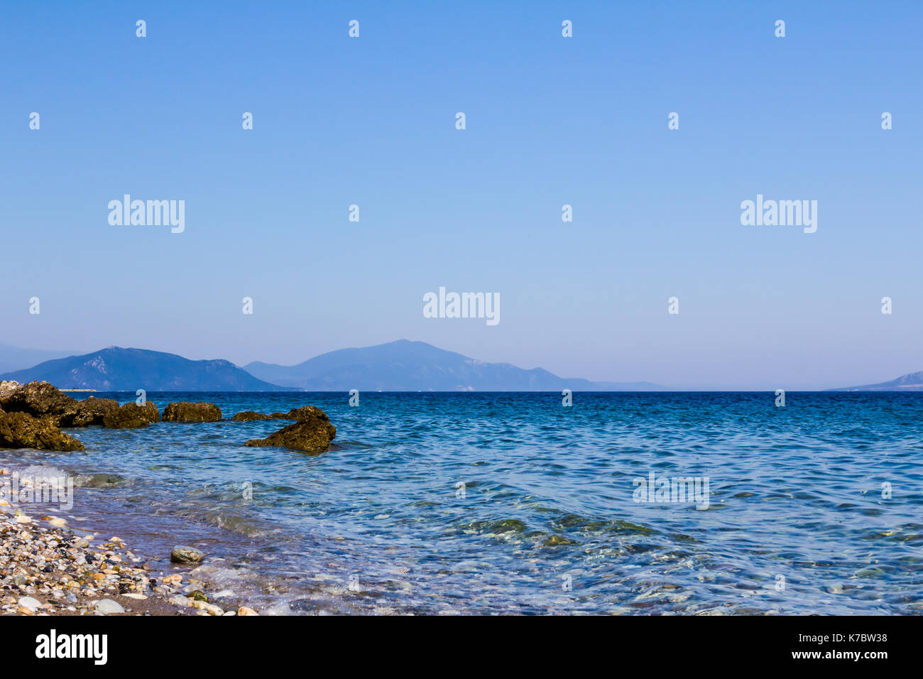 Rocky shore with boulder sticking out of shallow water surface with ...
