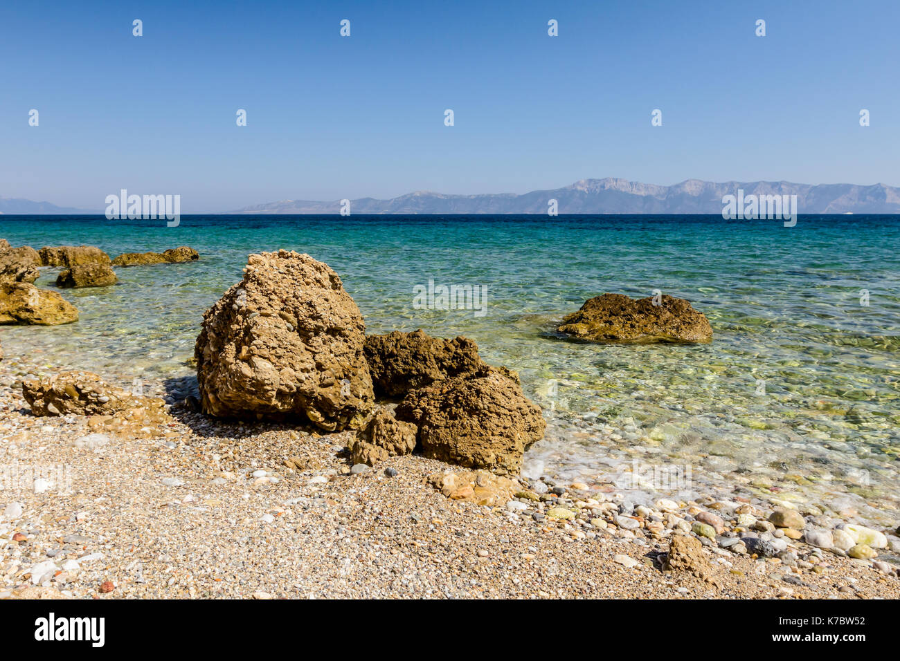 Rocky shore with boulder sticking out of shallow water surface with ...
