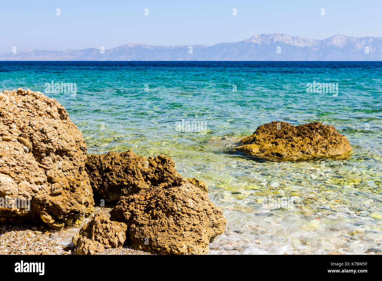 Rocky shore with boulder sticking out of shallow water surface with ...