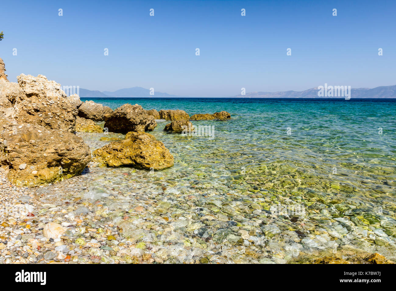 Rocky shore with boulder sticking out of shallow water surface with ...