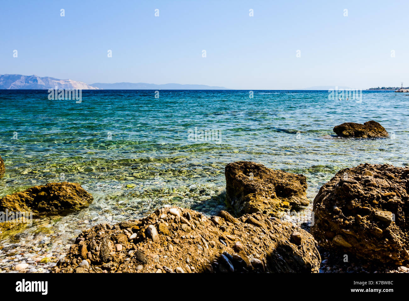 Rocky shore with boulder sticking out of shallow water surface with ...