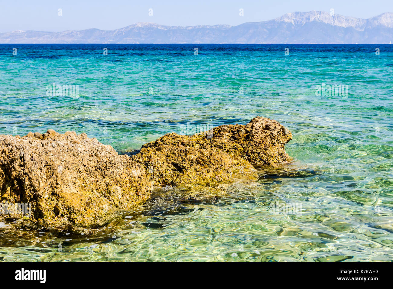 Rocky shore with boulder sticking out of shallow water surface with ...