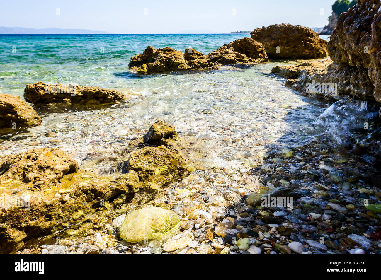 Rocky shore with boulder sticking out of shallow water surface with ...