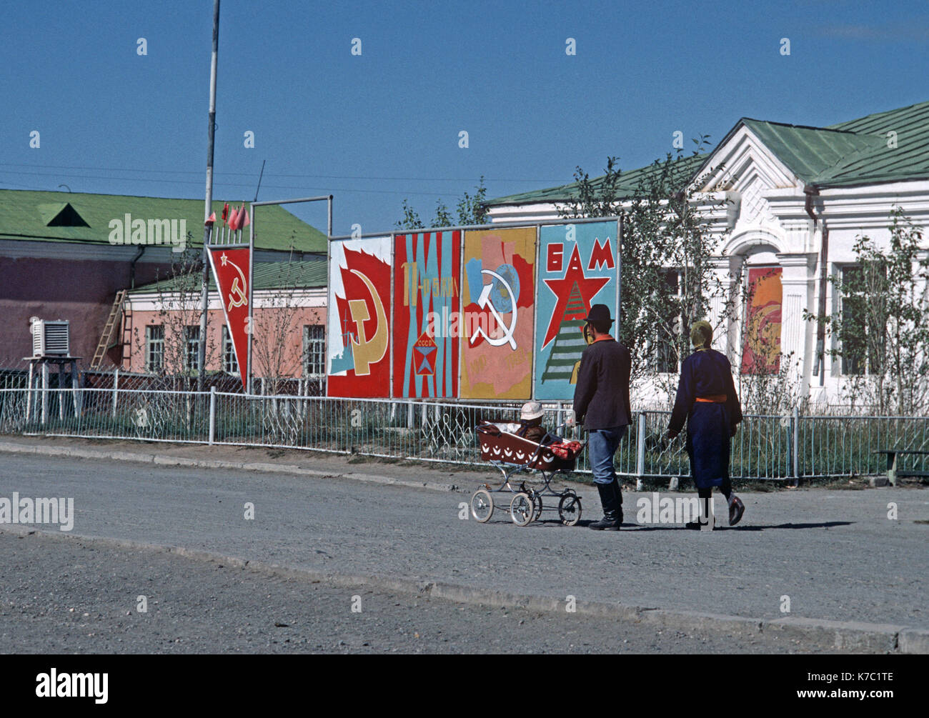 Couple with pram walking in front of Mongolian propaganda posters Gobi ...