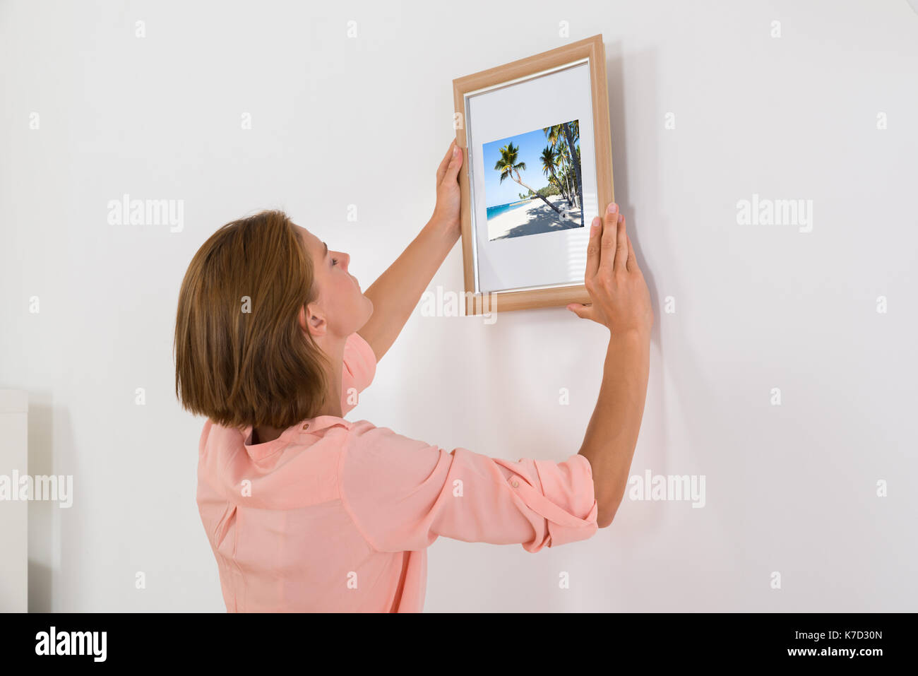 Young Woman Putting Photo Frame On White Wall Stock Photo - Alamy