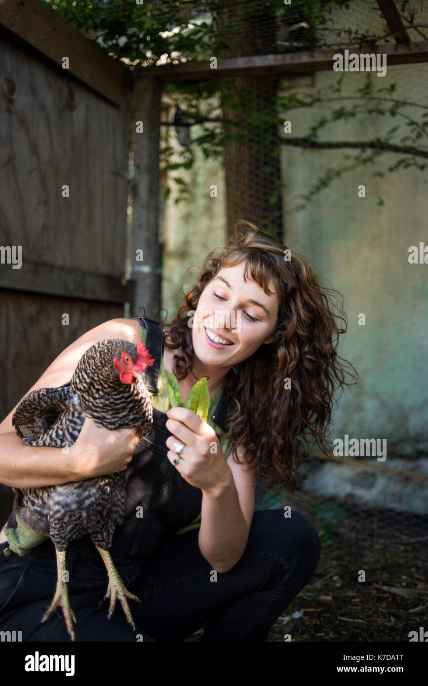 Happy woman feeding leaves to hen while crouching in poultry farm Stock ...