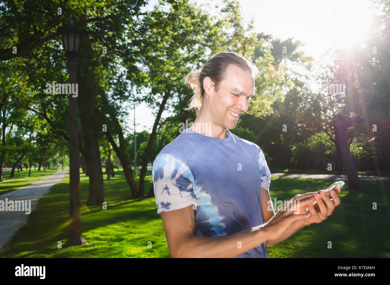 Happy man using mobile phone while standing in park Stock Photo - Alamy