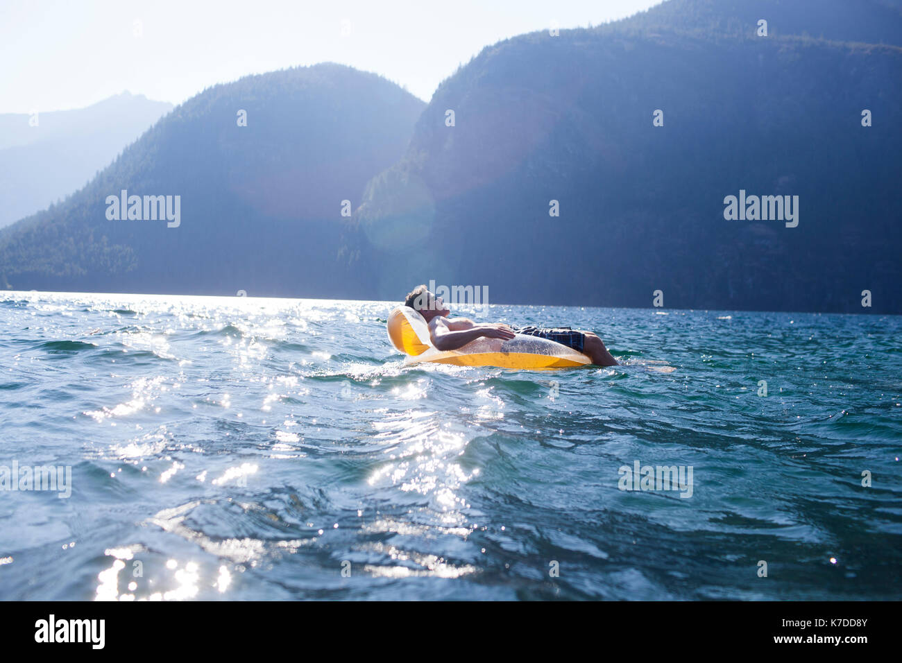 Side view of man lying on pool raft in lake against mountains during ...