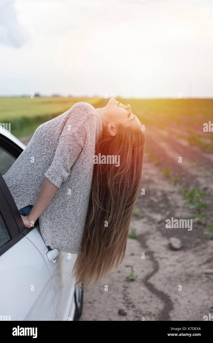 Side view of woman with long brown hair leaning out of car window on ...
