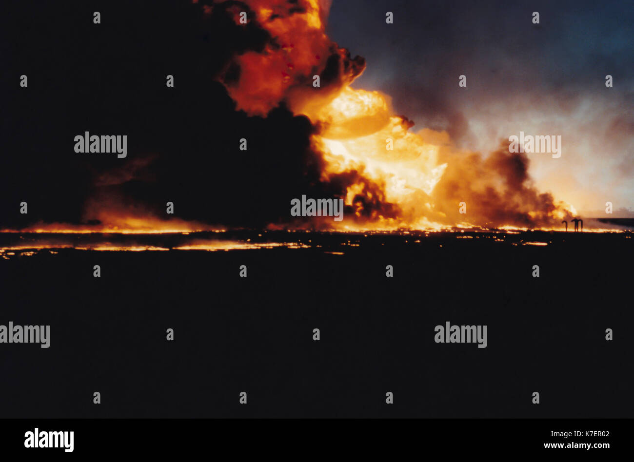 Burning oil well in field coated in spilled oil in aftermath of ...