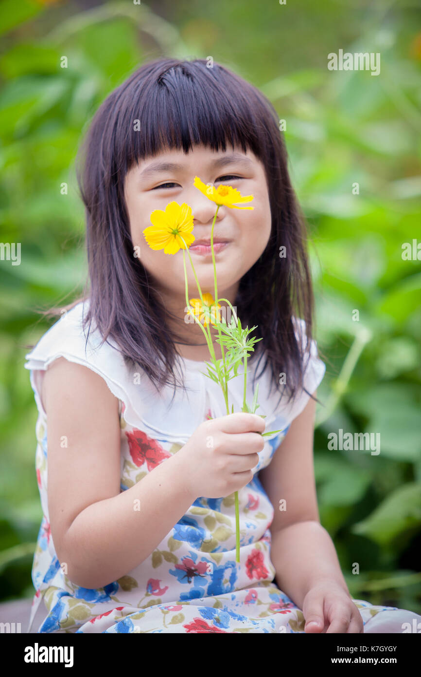 asian children sitting in garden with yellow cosmos flower in hand ...