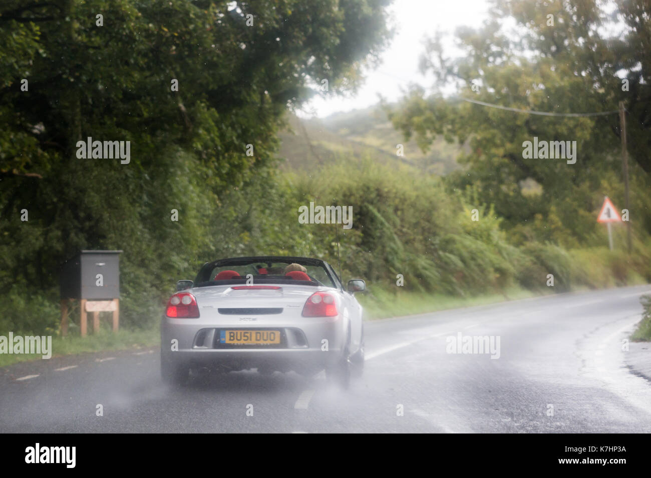 A motorist driving his open-top (convertible) car in the rain along the ...