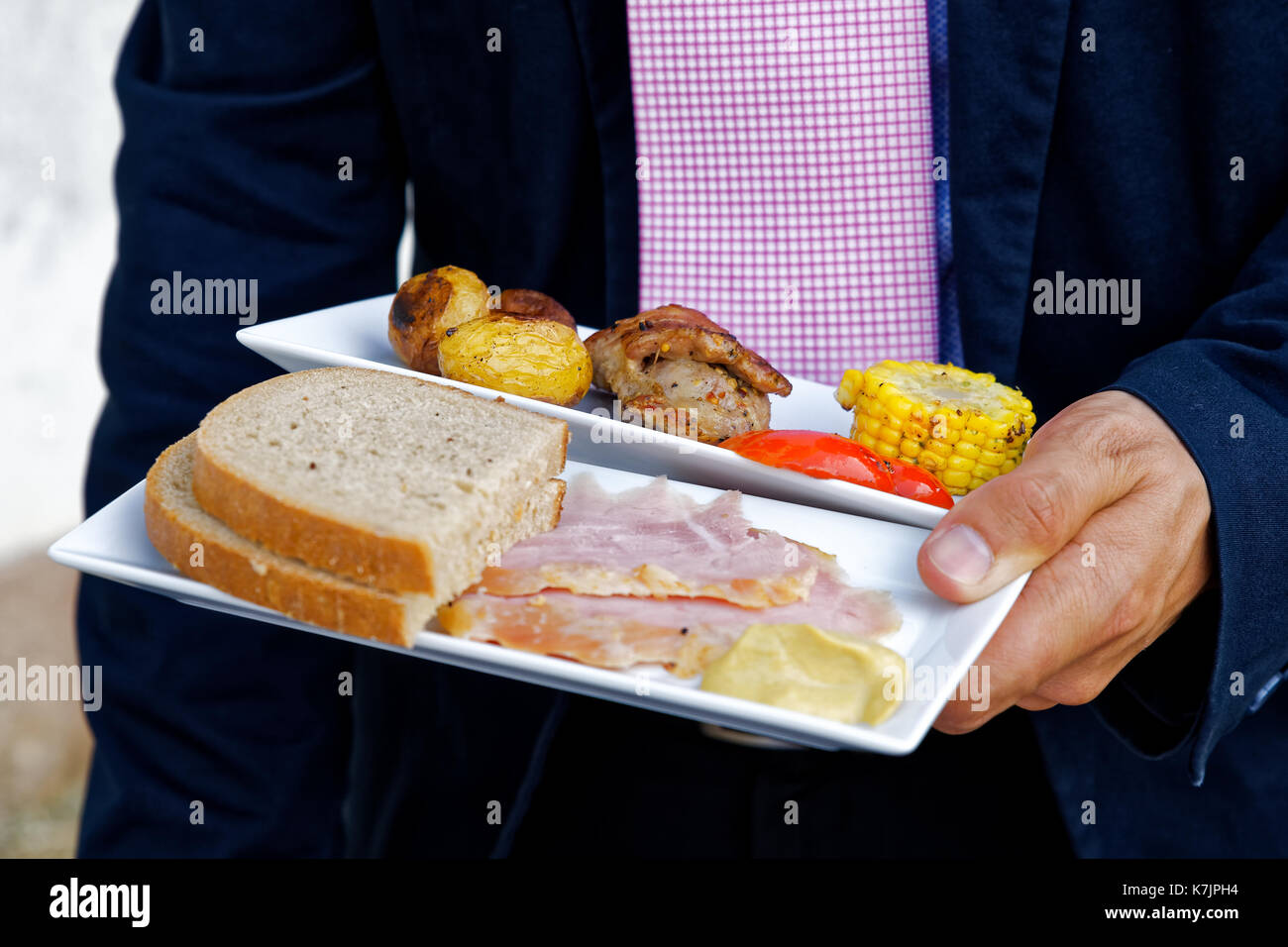 Man carrying white ceramic plates with grilled vegetables, bread, and ...